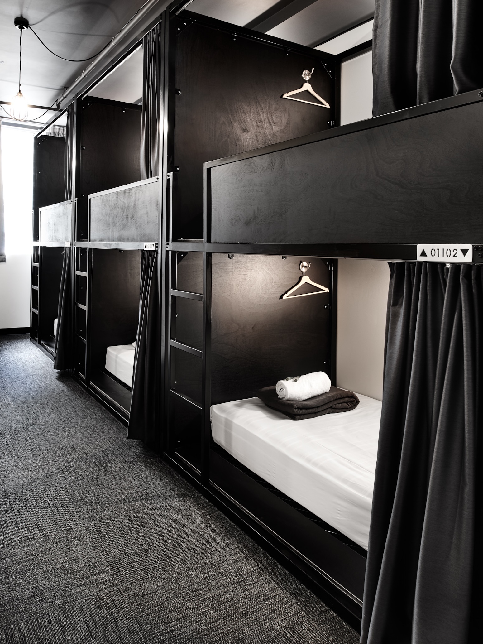 A row of capsule beds in a room with black walls at The Pod, Sydney ...