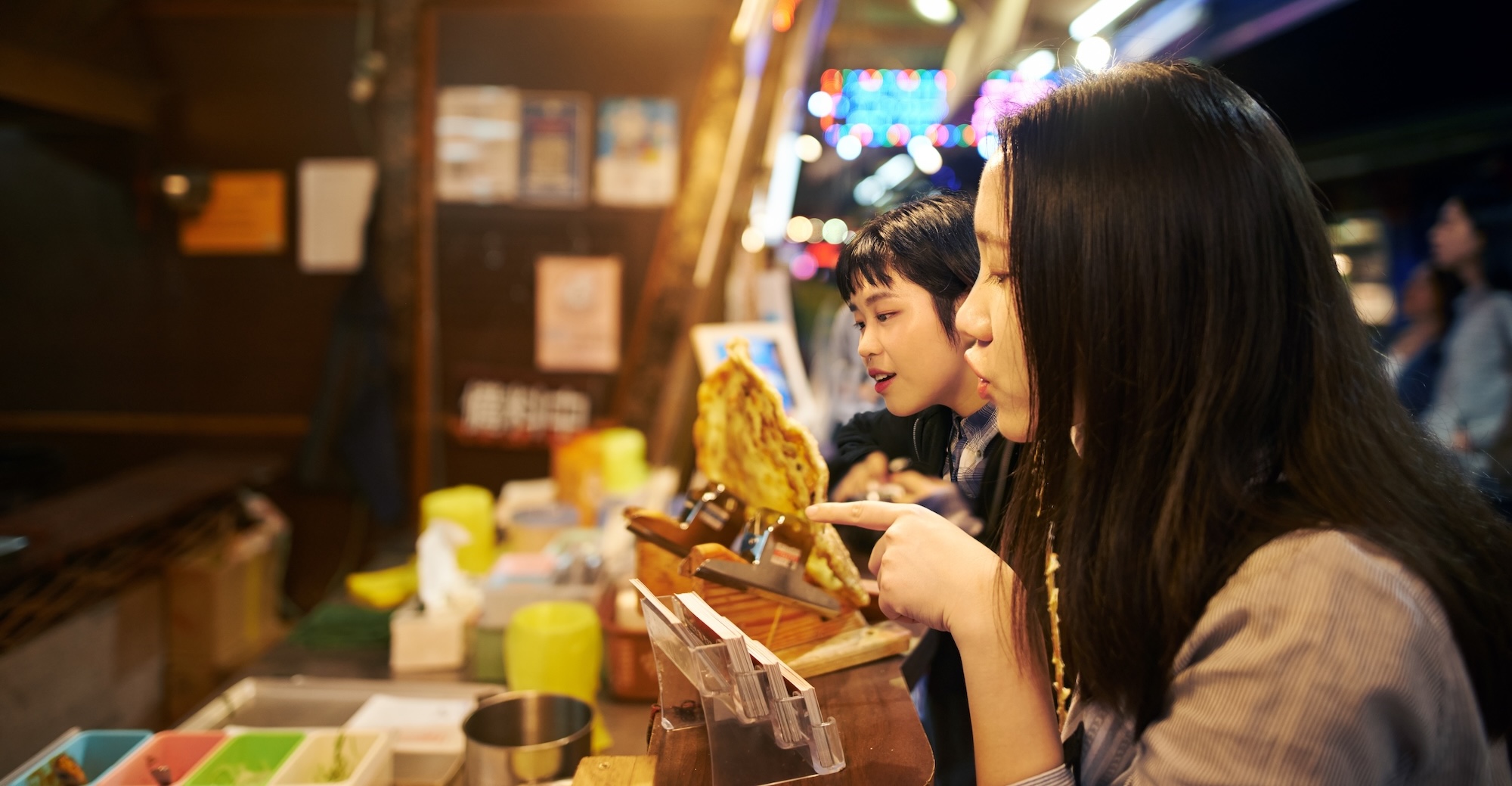Two women order meals at a food stand in a night market