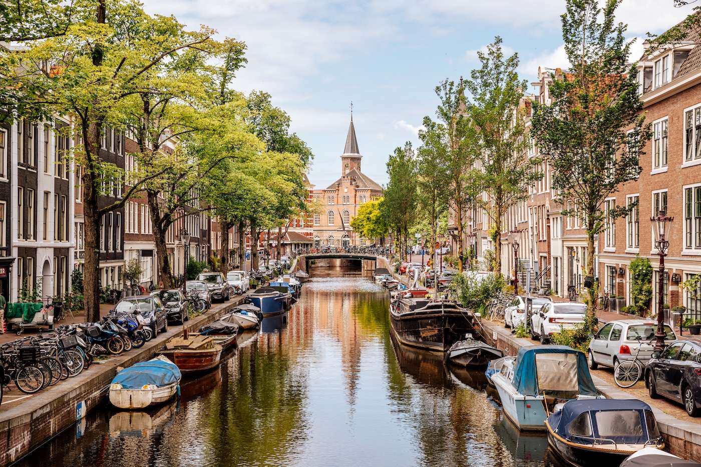 A canal is Amsterdam looks vibrant with bikes and cars parked up either ...